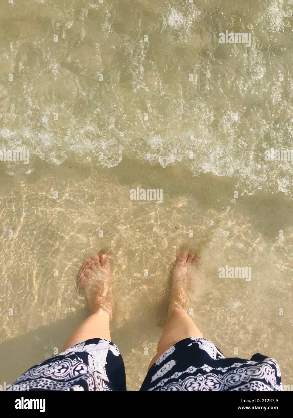 A man standing in the shoreline of a tropical beach, with the water ...