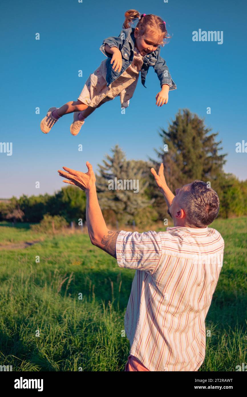 A young man tosses his daughter up and she laughs with happiness. Dad ...