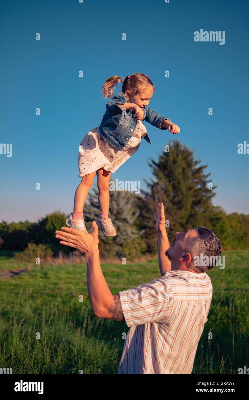 A young man tosses his daughter up and she laughs with happiness. Dad ...