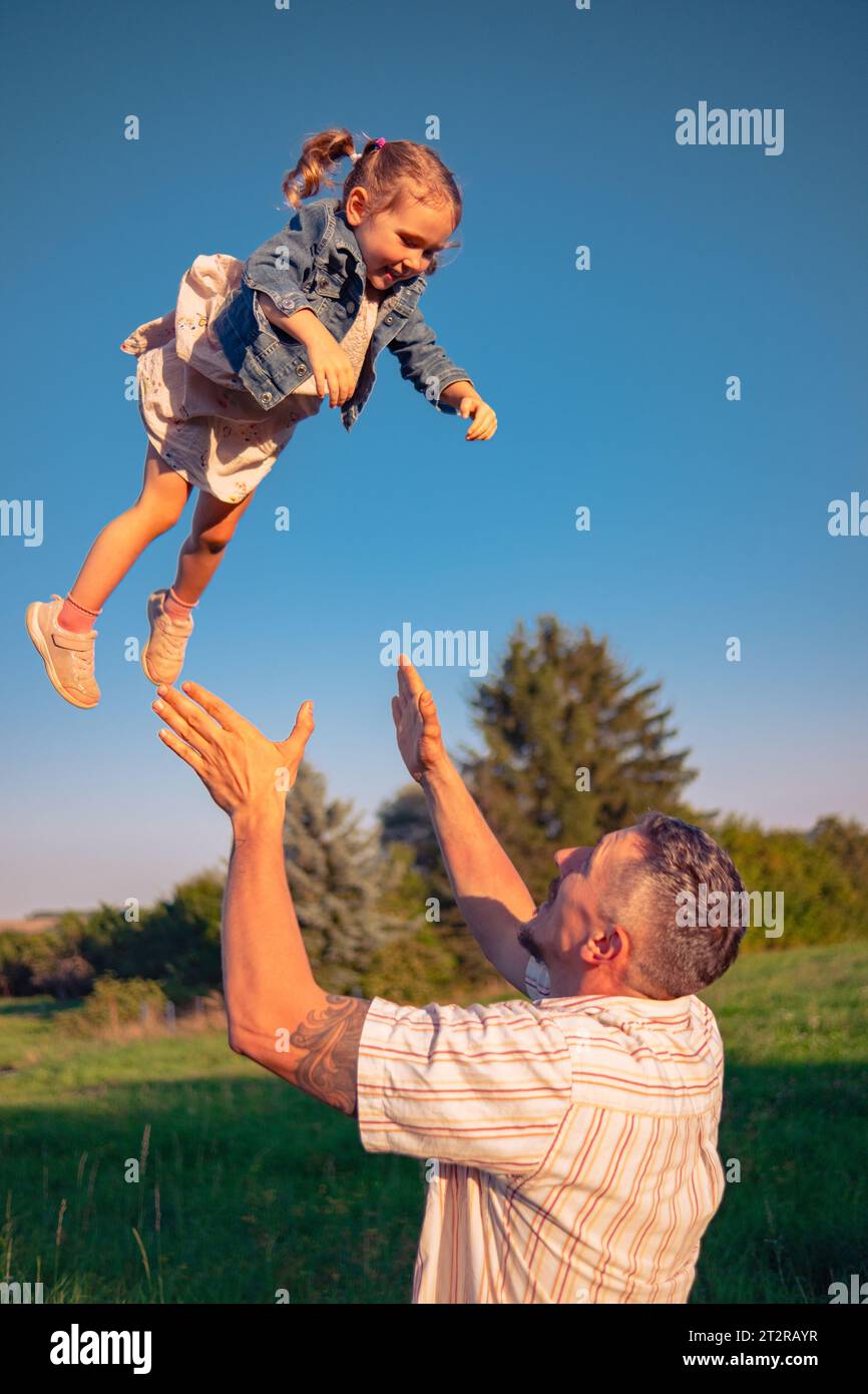 A young man tosses his daughter up and she laughs with happiness. Dad ...
