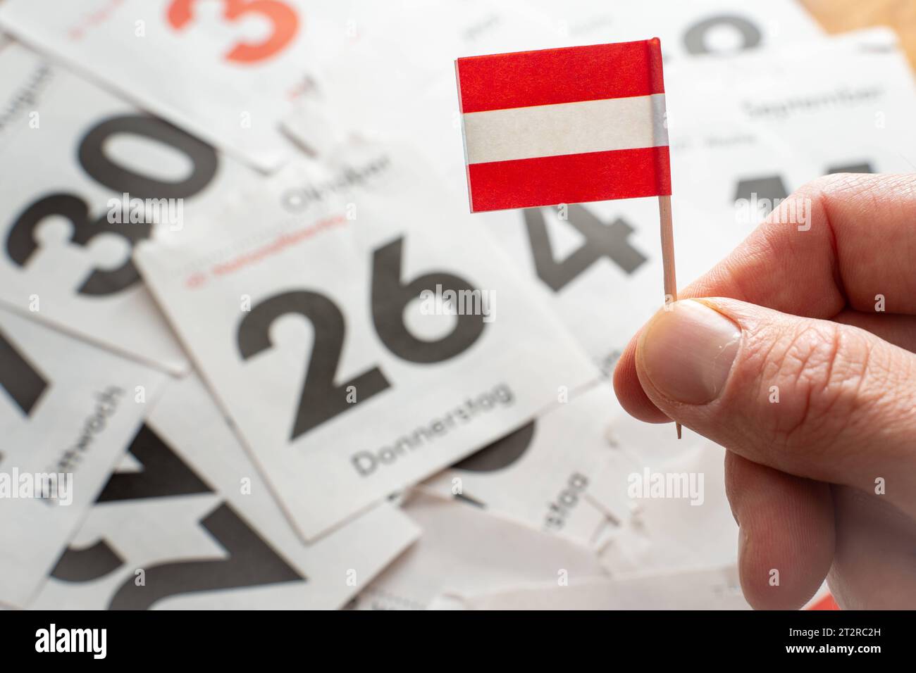 Hand holding Austrian national flag in front of calendar pages with ...