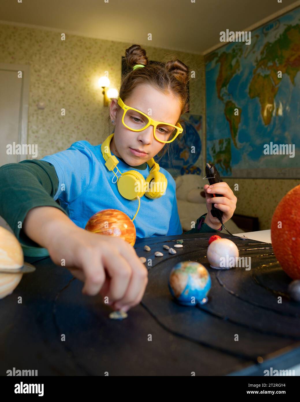 Focused girl in vibrant attire, working on her tabletop solar system ...
