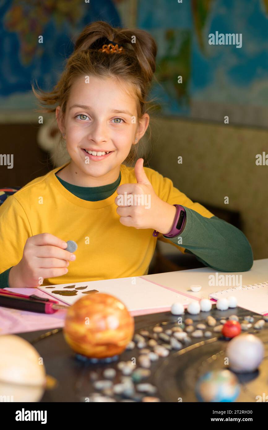 Joyful young girl giving a thumbs up, amidst her artistic solar system ...