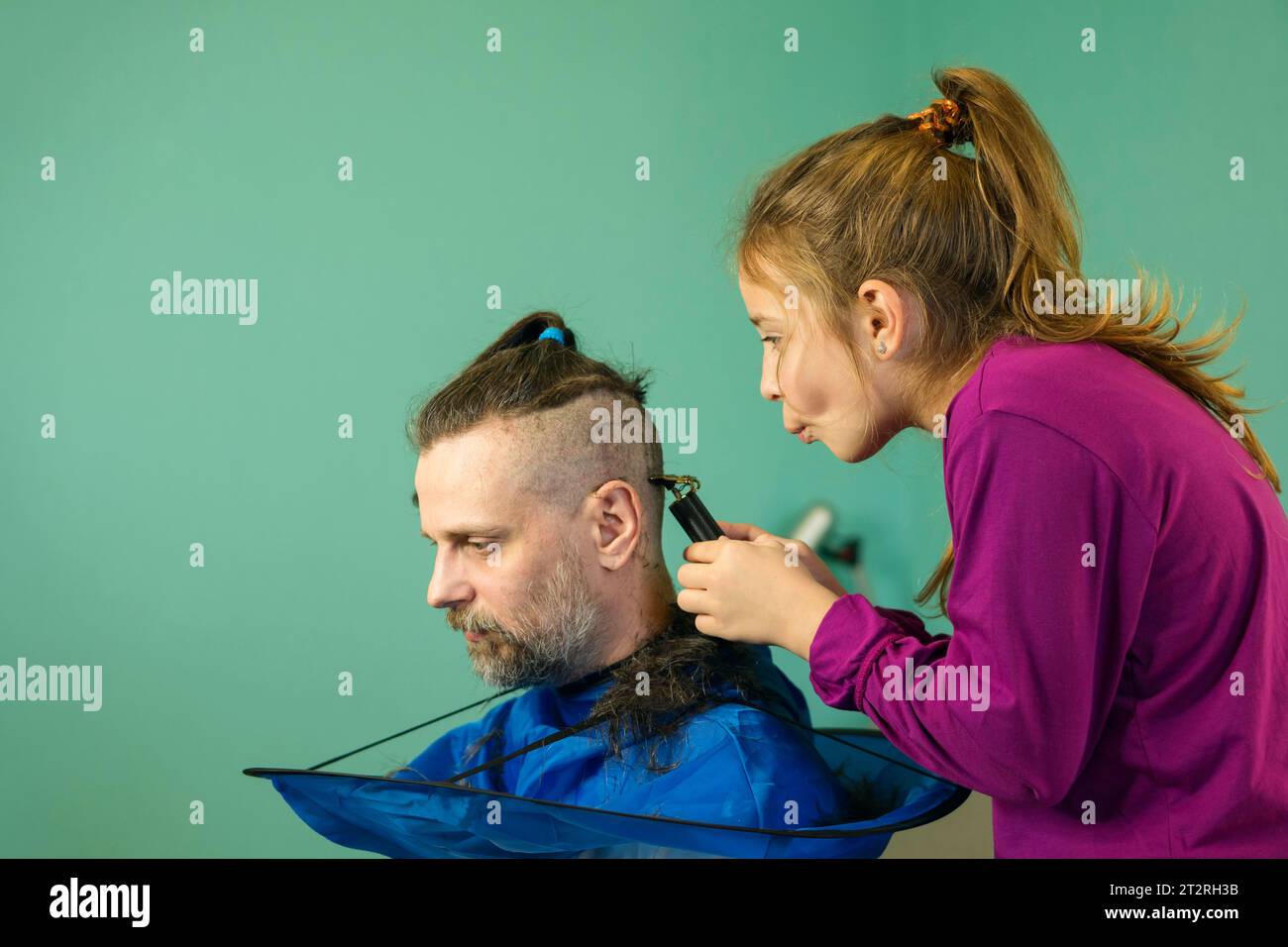 Joyful girl playfully cuts her father's hair at home, creating a bond ...
