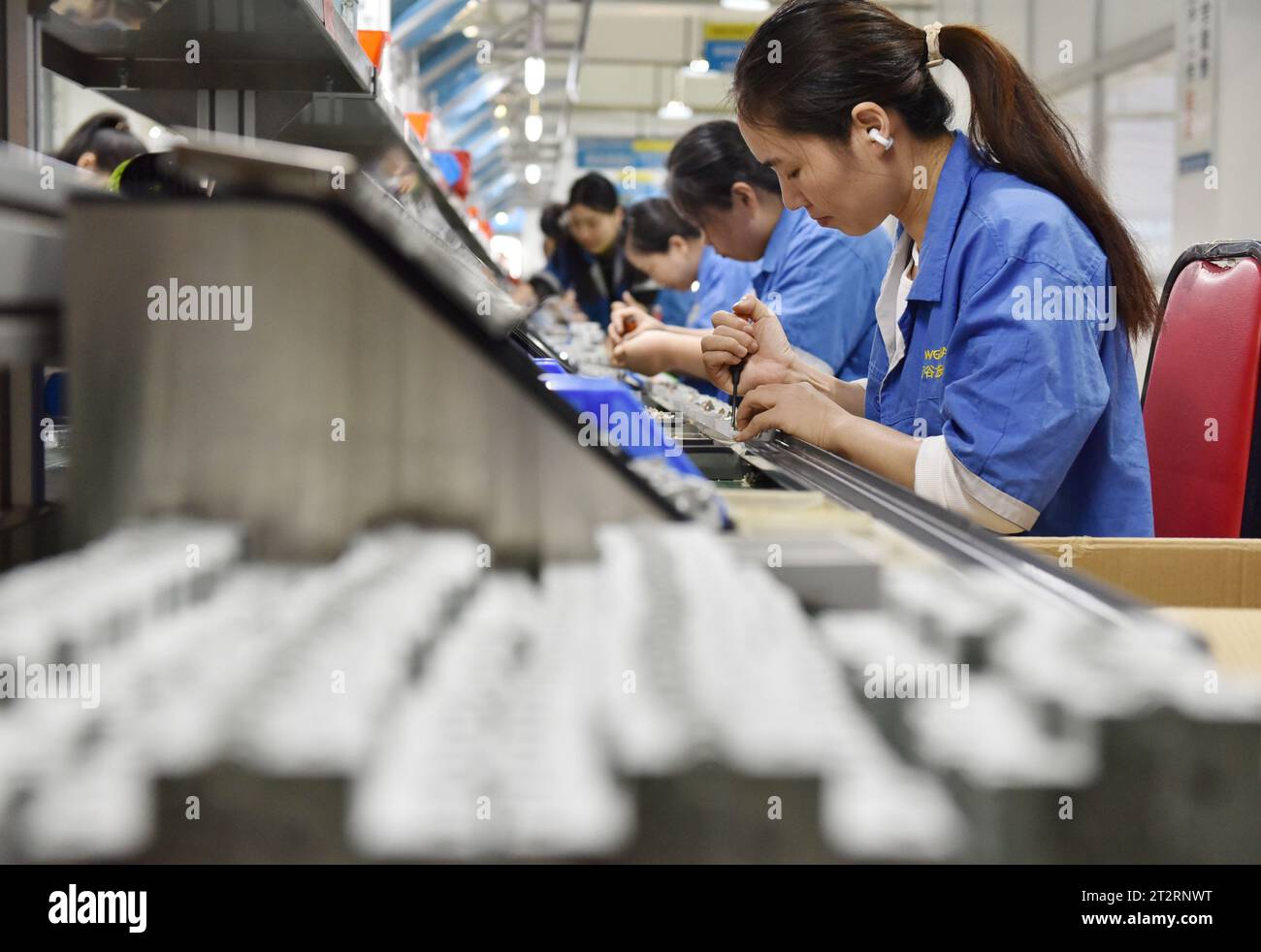 Women wearing blue overalls work on the assembly line of a factory that ...