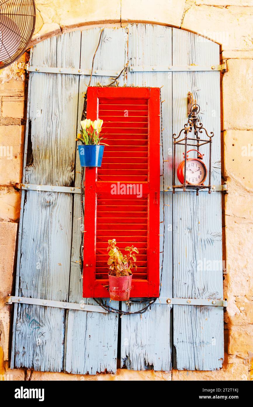Red shutter on old blue door as decoration. With clock and flower pots ...