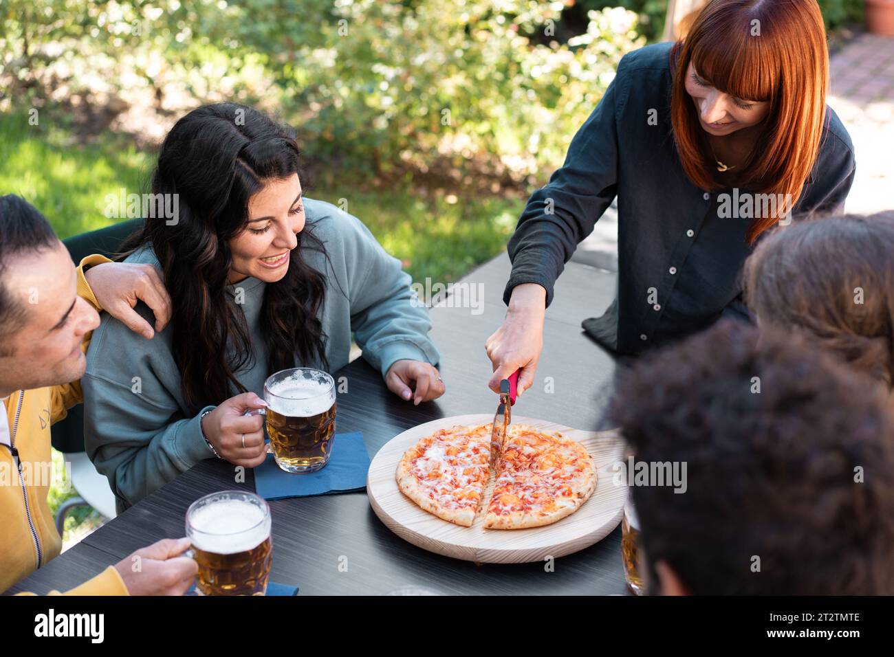 A young woman masterfully slices a freshly baked pizza, as friends ...