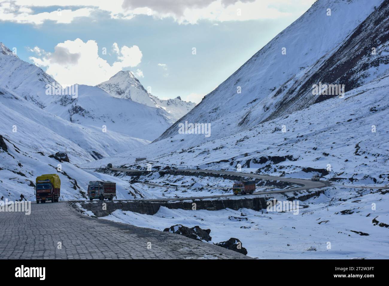 Trucks carrying goods move along the snow covered mountains in Drass, a ...
