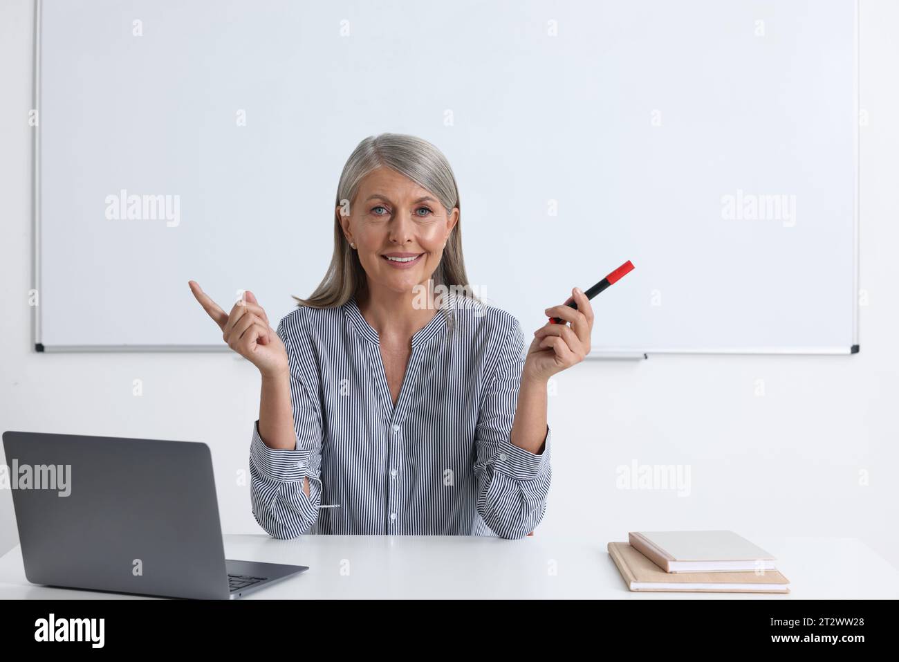 Happy professor giving lecture near laptop at desk in classroom Stock Photo - Alamy