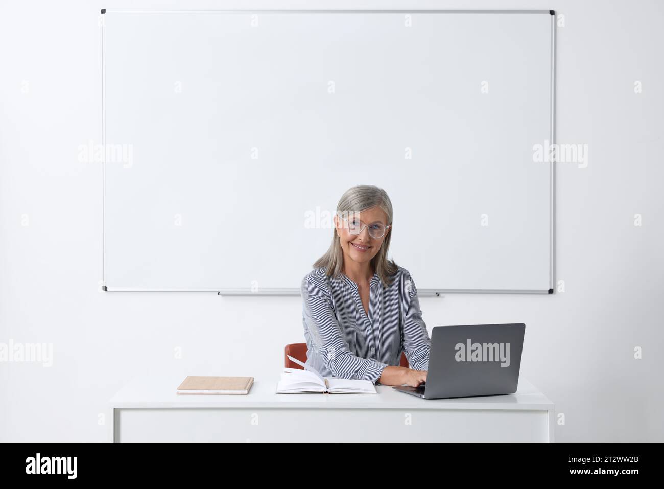 Happy professor giving lecture while using laptop at desk in classroom ...