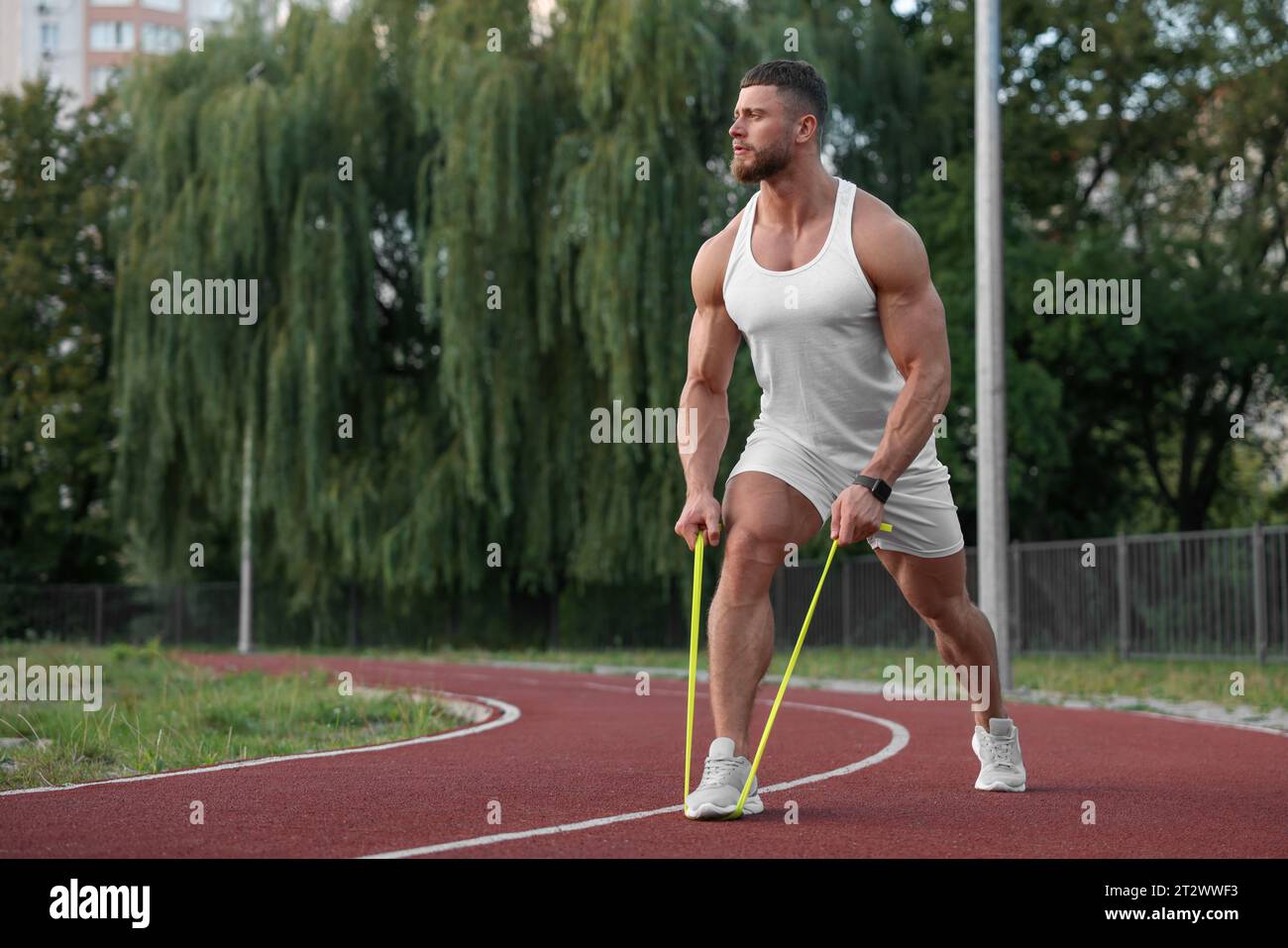 Muscular man doing exercise with elastic resistance band at stadium ...