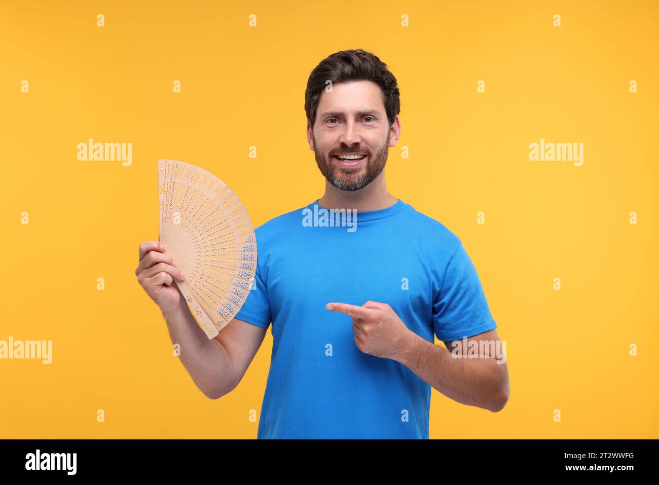 Happy man holding hand fan on orange background Stock Photo - Alamy