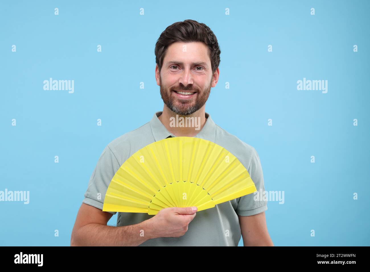 Happy man holding hand fan on light blue background Stock Photo - Alamy