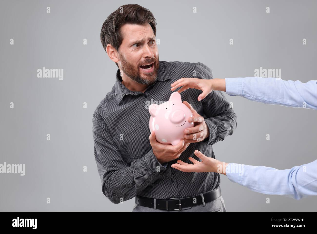 Scared man trying to protect piggy bank from woman on light grey ...