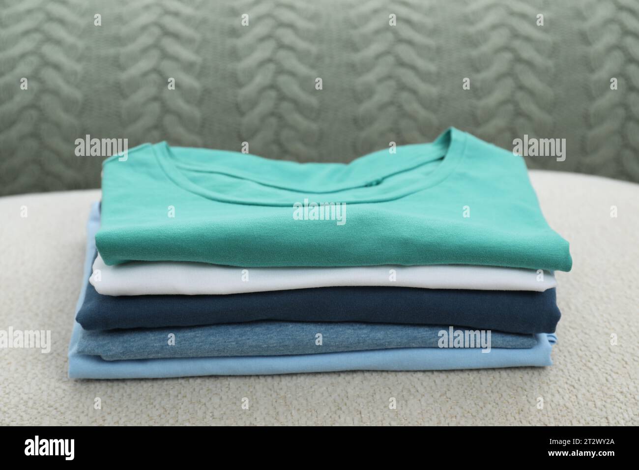 Sorting and organizing. Stack of different folded clothes on ottoman ...