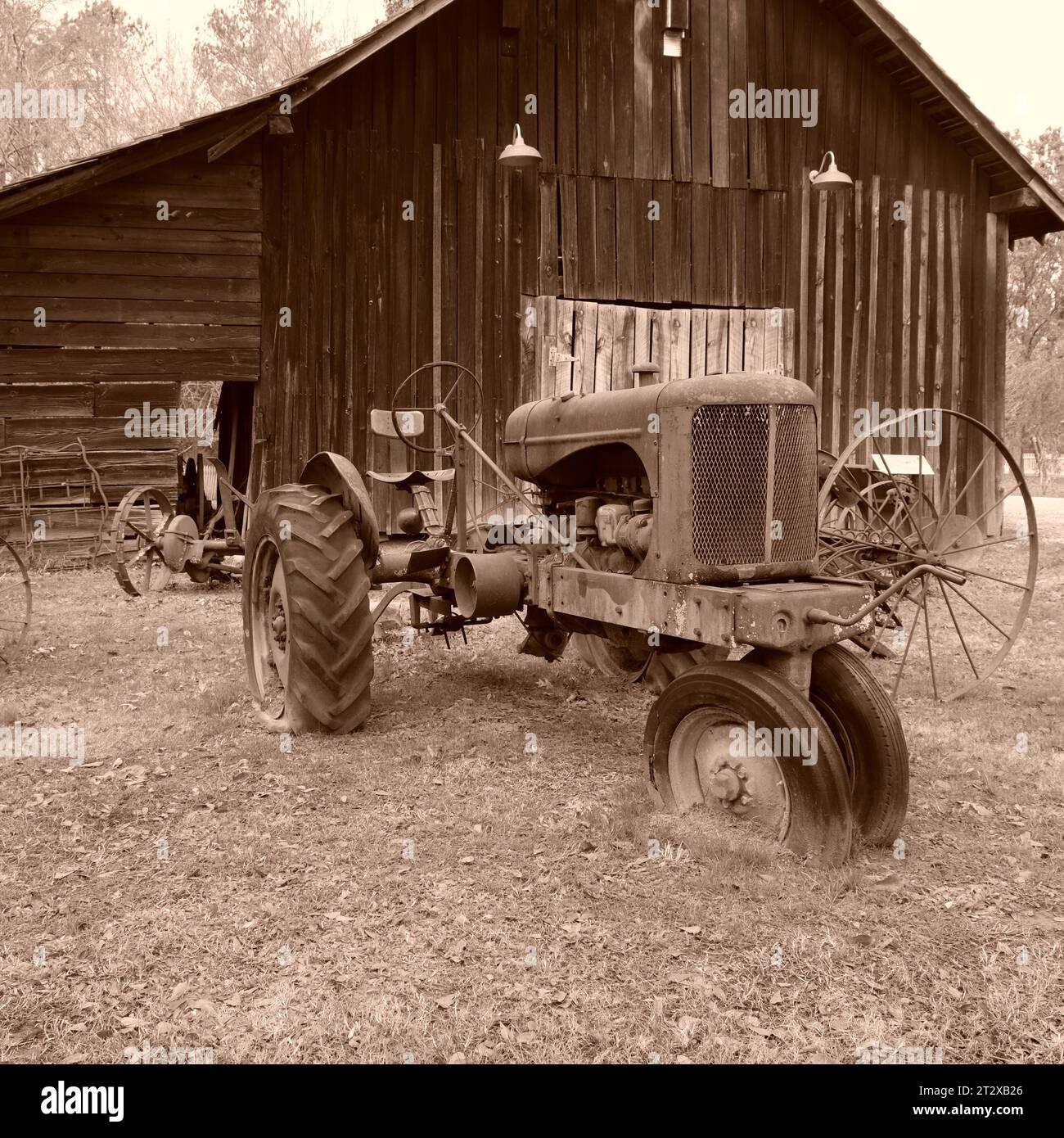 A sepia shot of an antique tractor in front of a barn with a variety of ...
