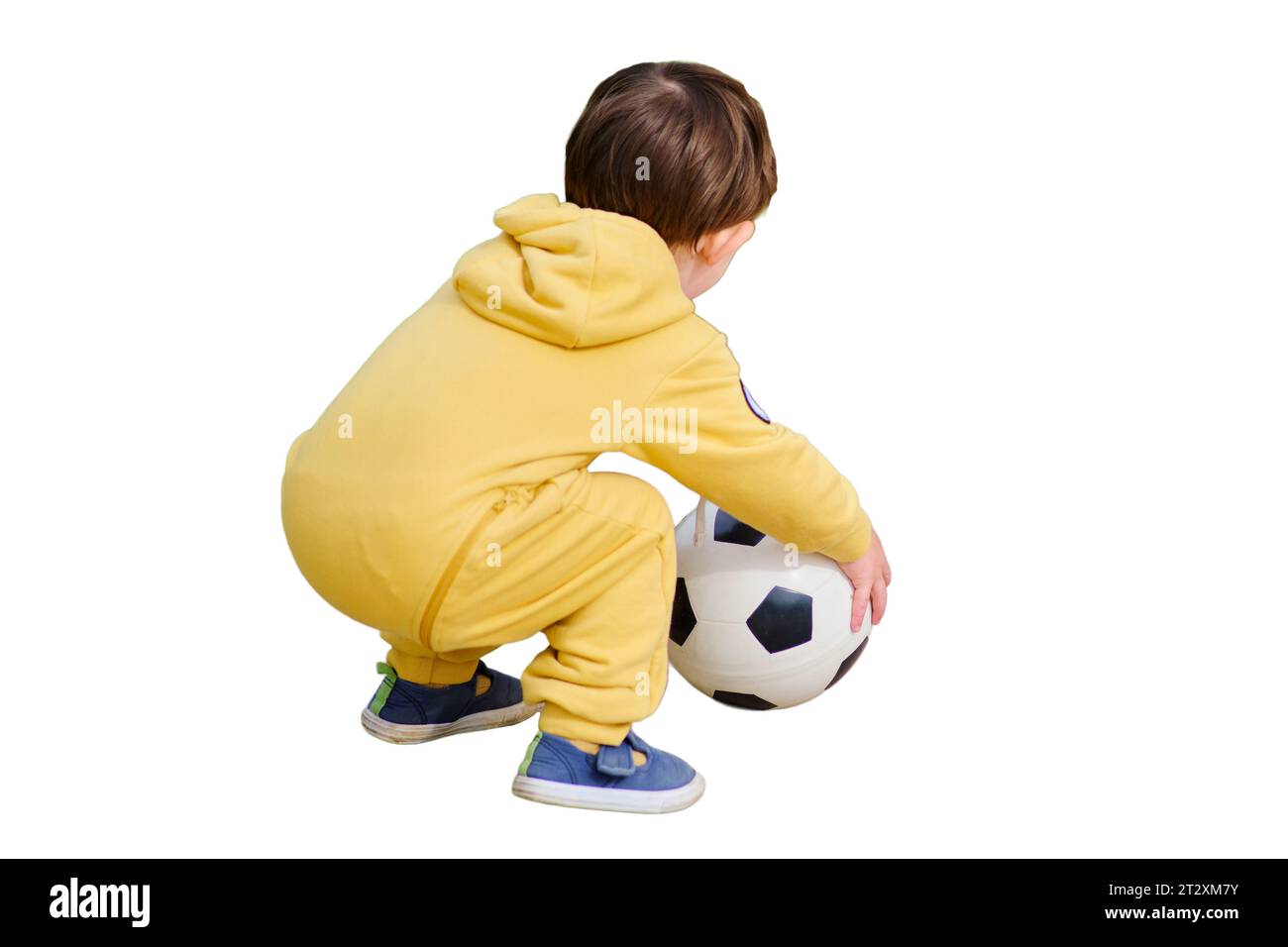 A toddler baby is kicking a football on the green grass in the park ...