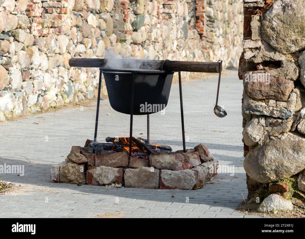 a photo of a metal pot on a fire, a soup cooker outside, cooking in the ...