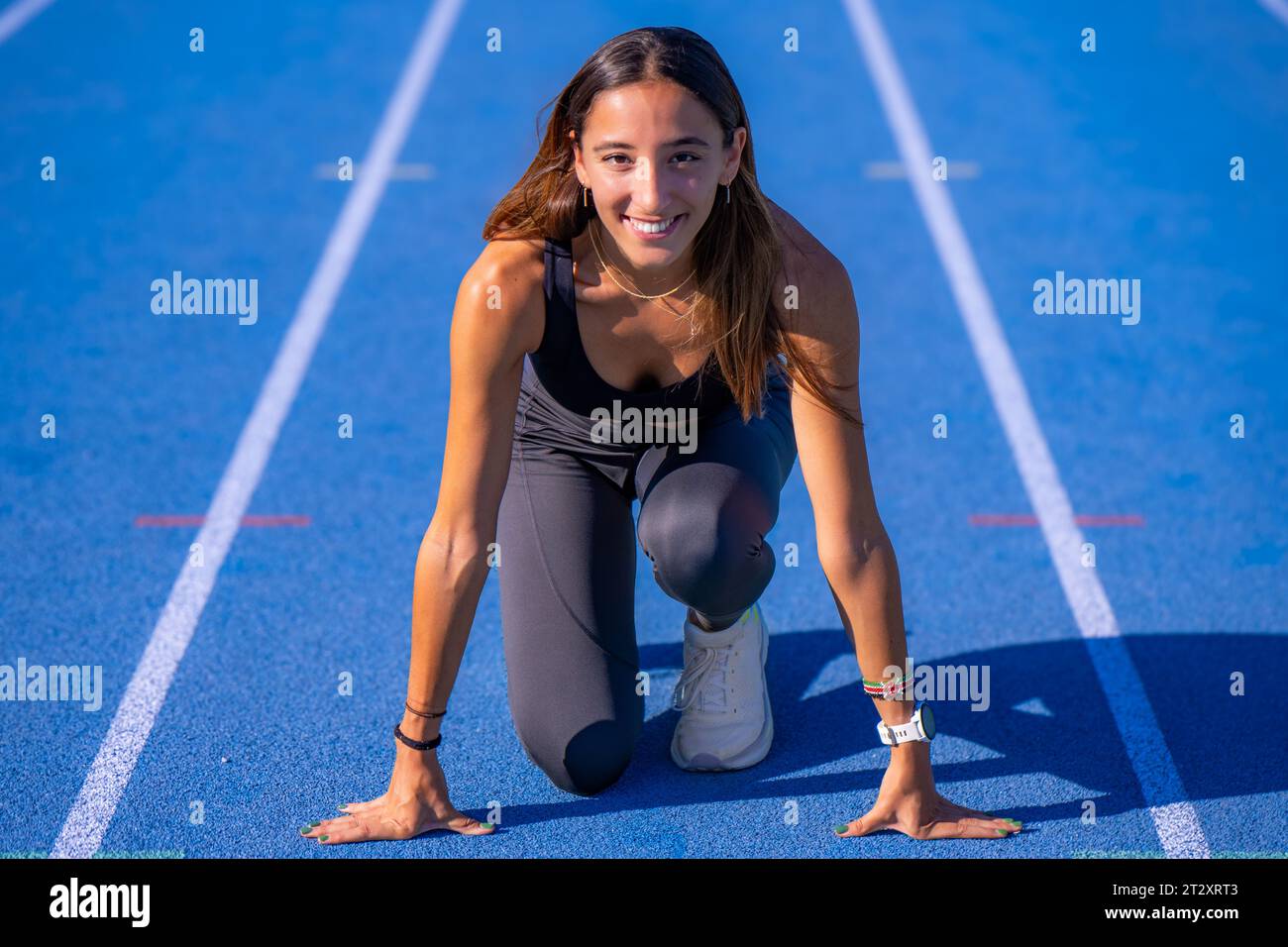 Beautiful young runner, tanned with long dark hair, smiling on a blue ...