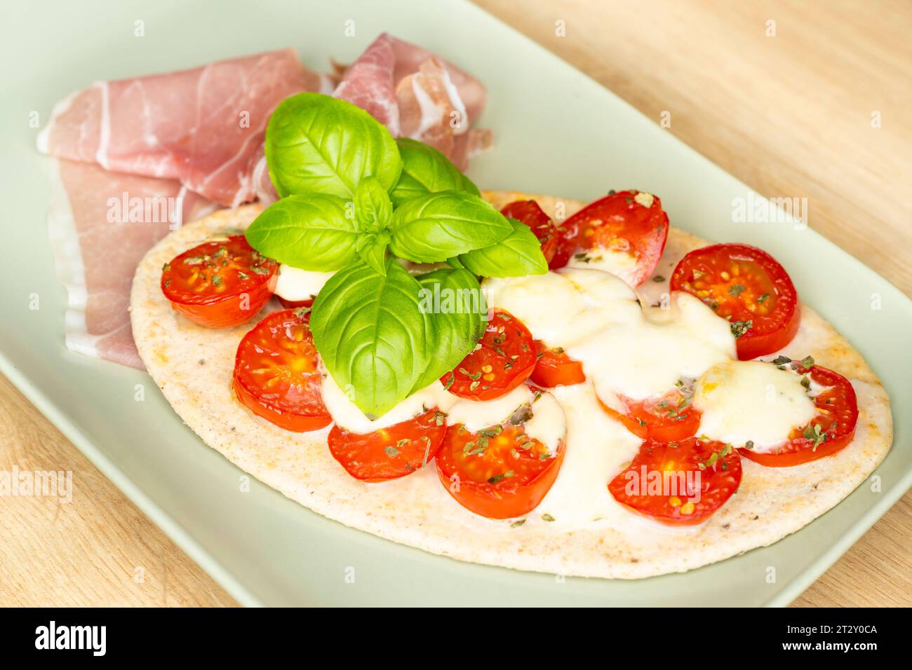 Flatbread with cherry tomatoes, mozzarella, basil leaves and fresh prosciutto on a rectangular ...