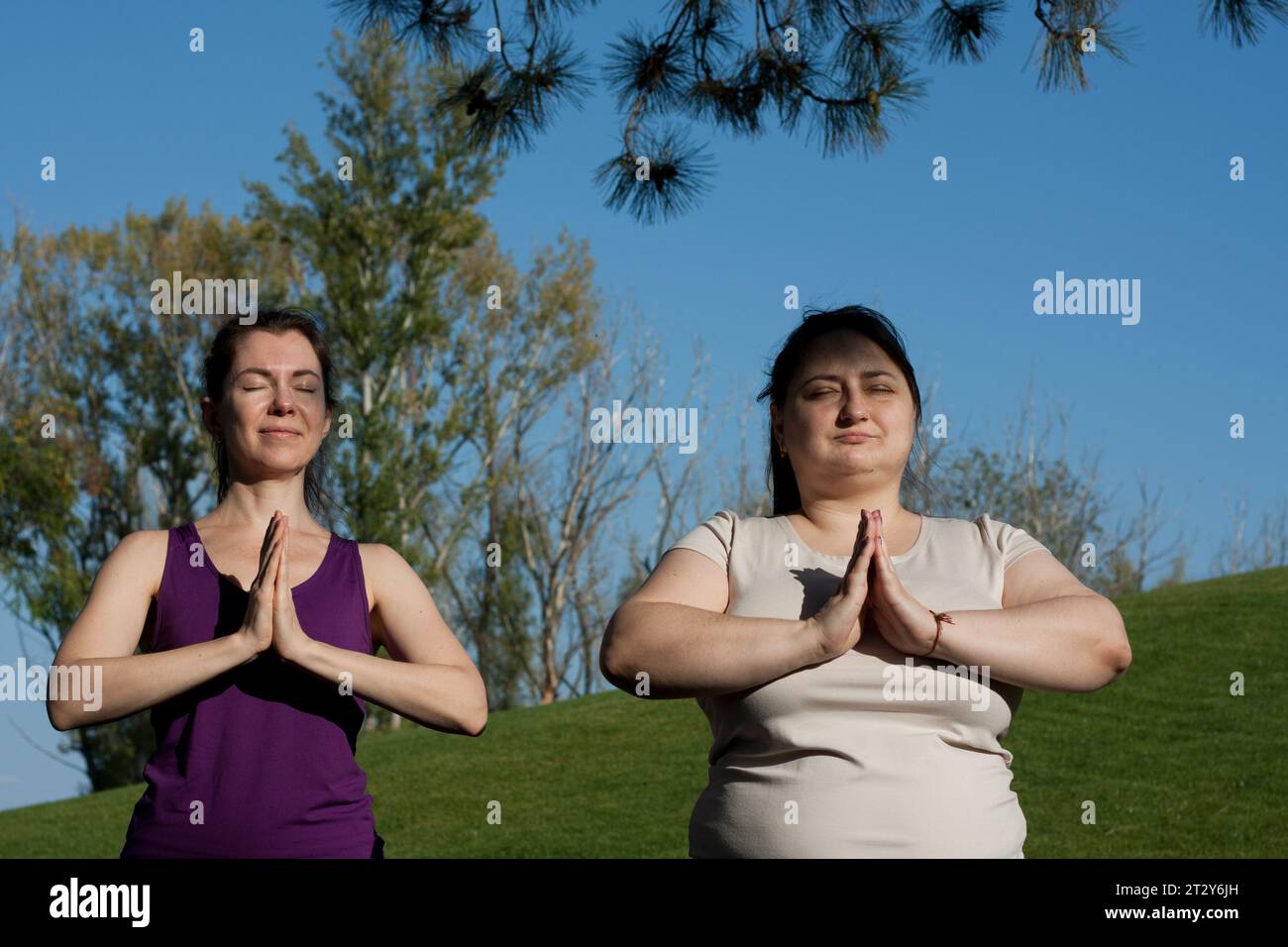 Two middle-aged women practice yoga in city park, meditate, standing ...
