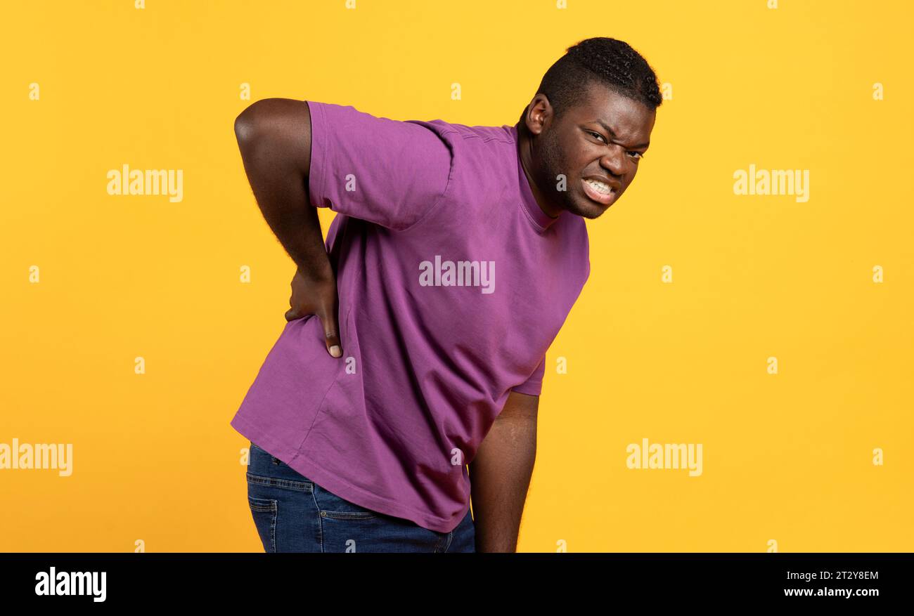 Unhappy black guy touching his aching lower back, yellow background ...