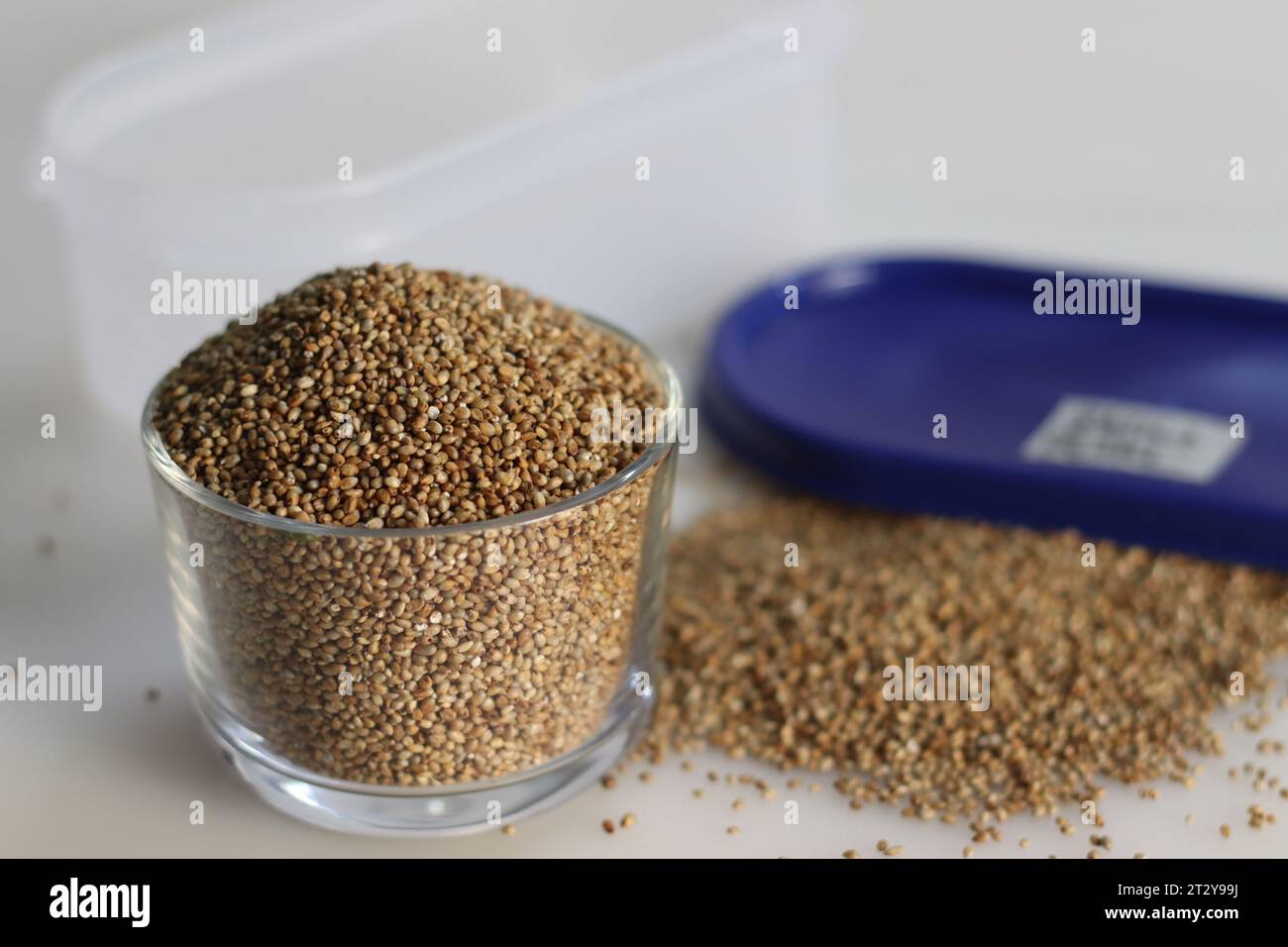 Pearl millet grains in a storage container and glass bowl filled to the ...