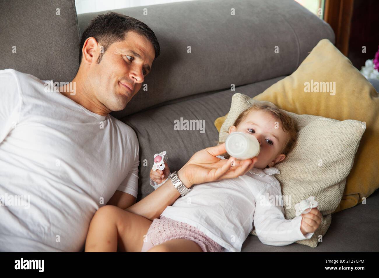 Young father giving bottle to his baby in a relaxed position on the ...