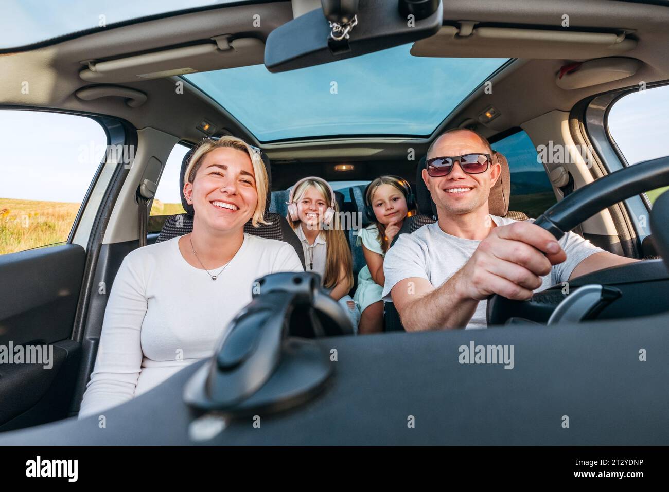 Happy young couple with two daughters inside car during auto trop. They are smiling, laughing ...