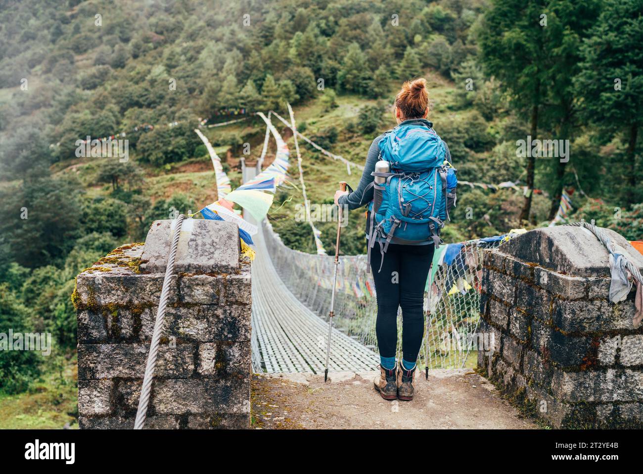 Young female crossing canyon over Suspension Bridge with multicolored ...