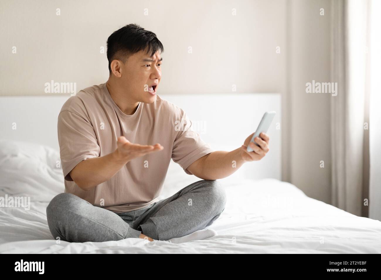 Angry mature asian man sitting on bed with phone Stock Photo - Alamy