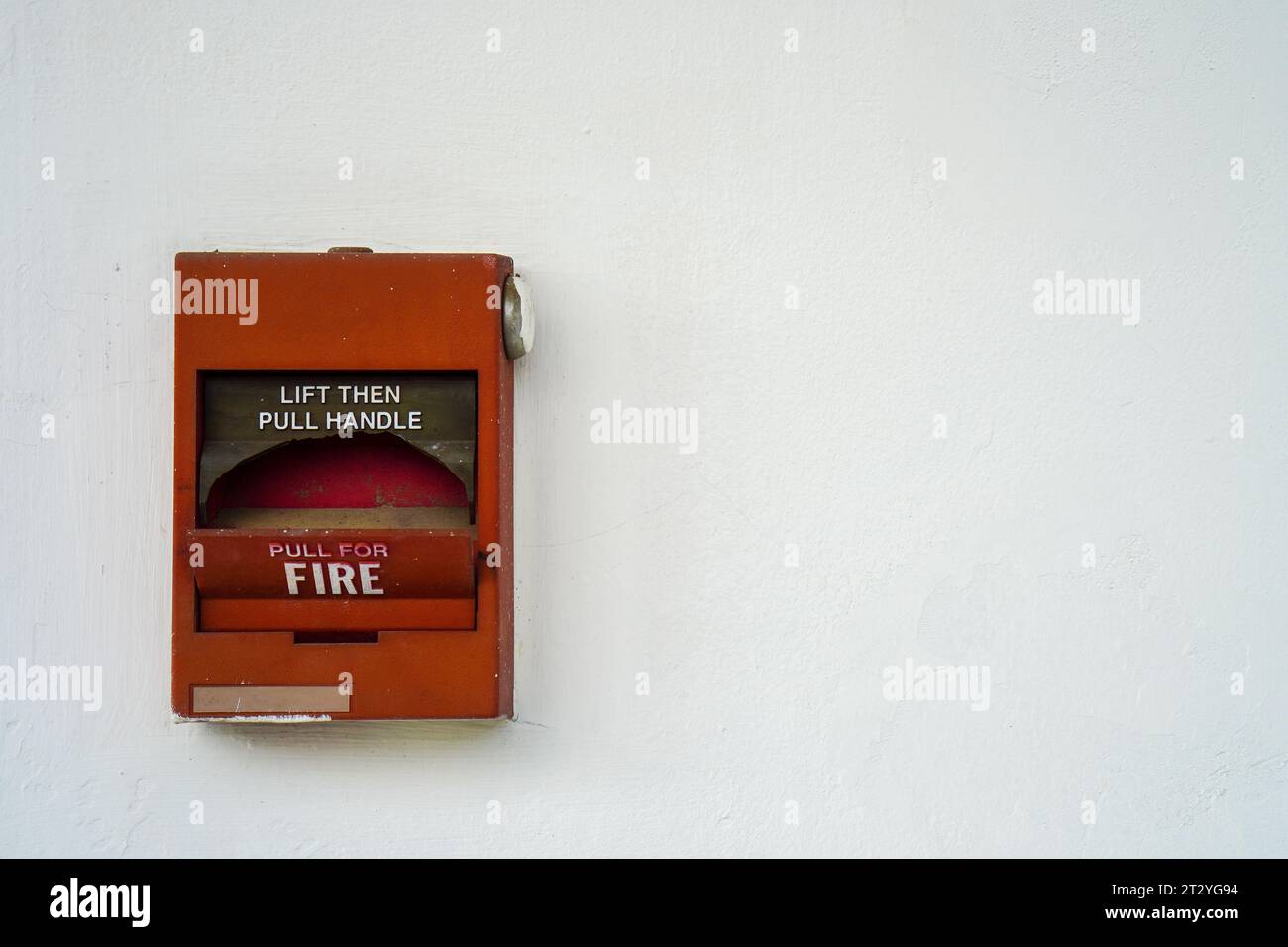 Damaged red fire alarm box with clean white wall as background with ...