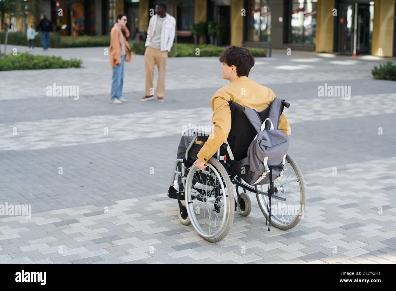 Rear view of young man with disability moving in wheelchair in the city ...