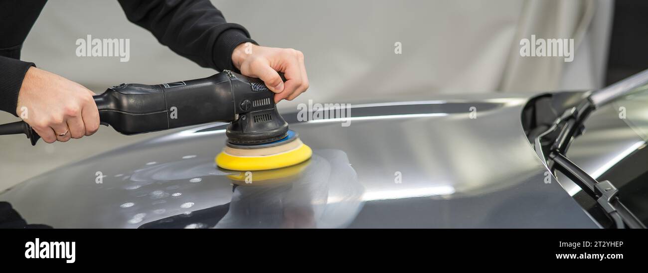 A mechanic polishes the surface of the hood of a gray car. Widescreen ...