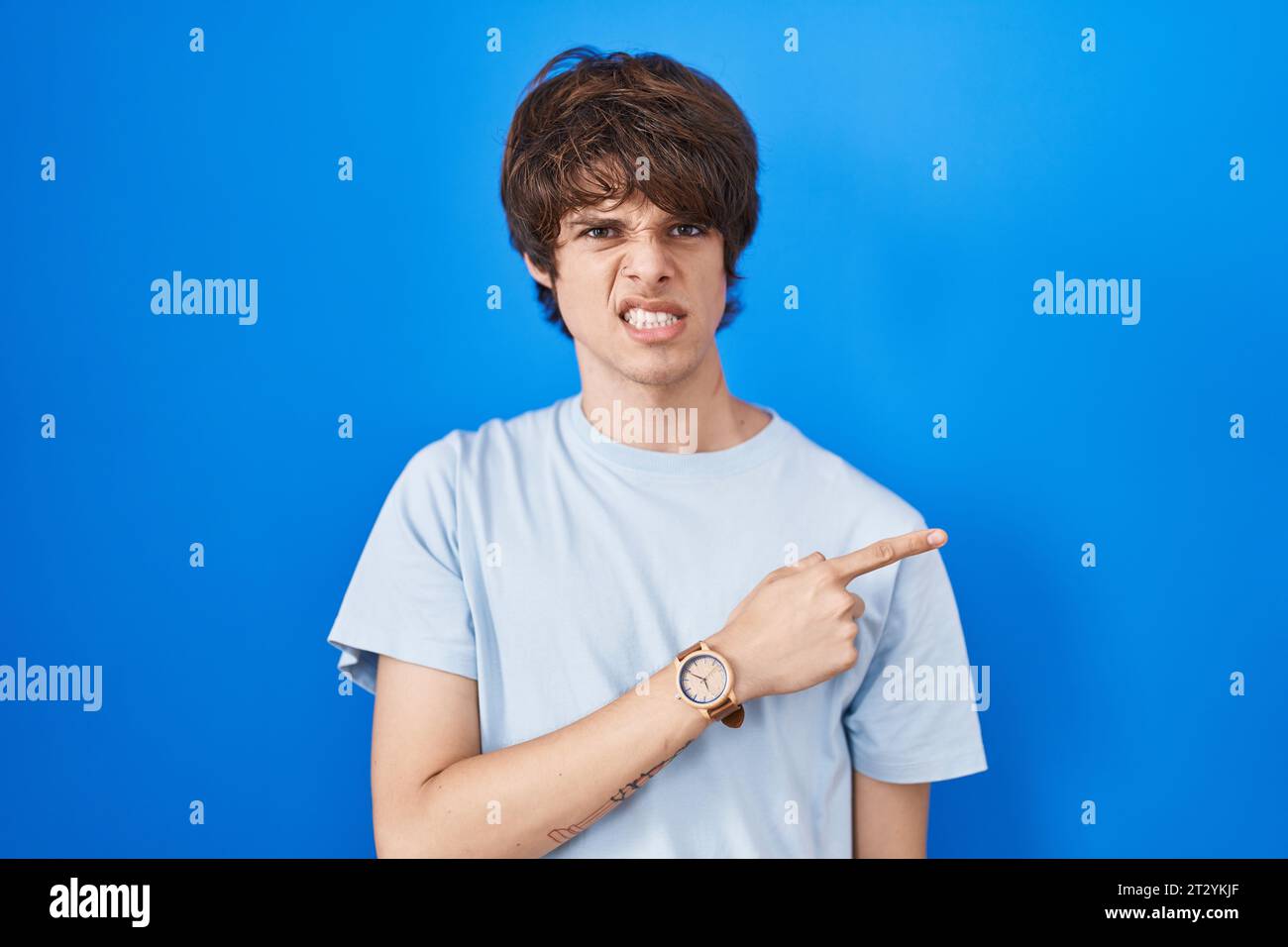 Hispanic young man standing over blue background pointing aside worried ...