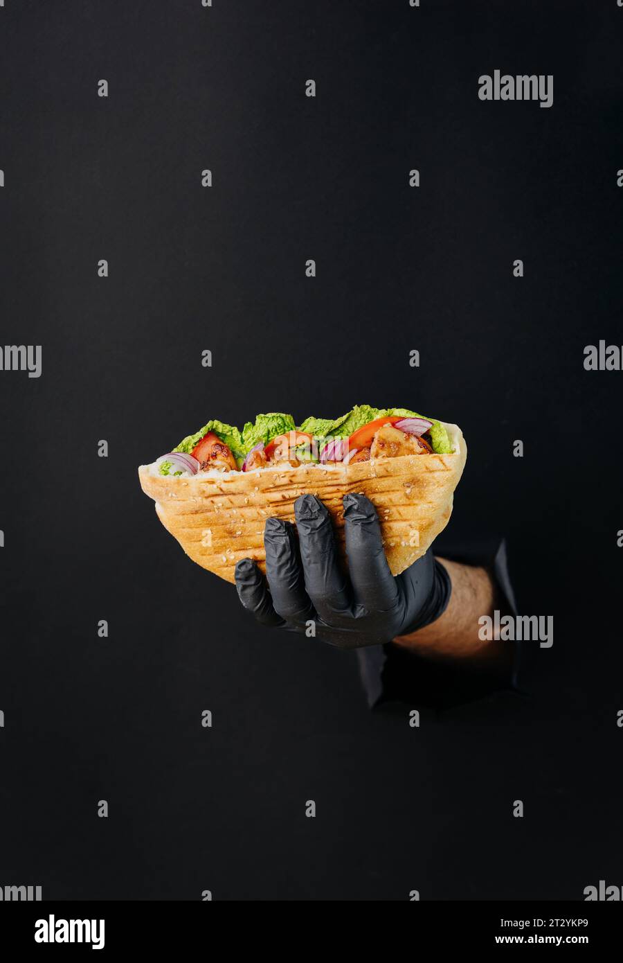 Cooks hand holding doner kebab through torn holes on black paper ...