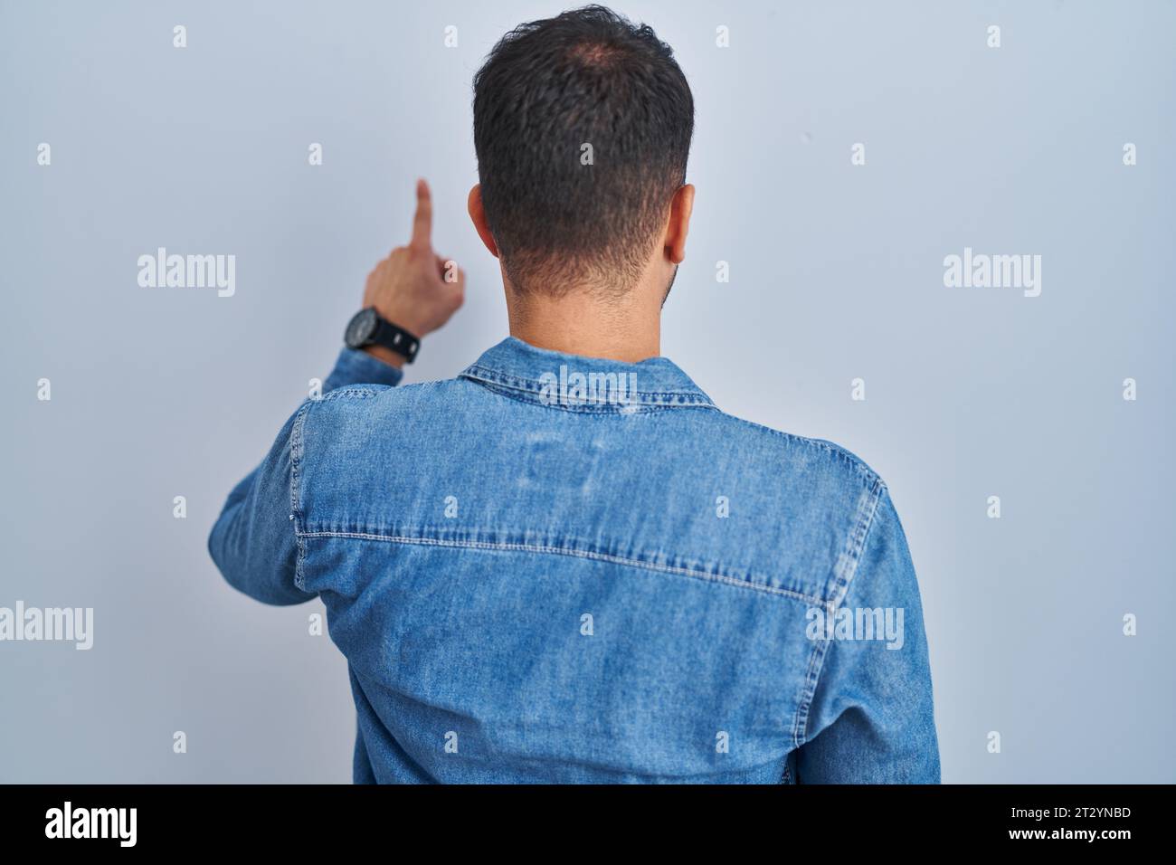 Young hispanic man standing over blue background posing backwards ...