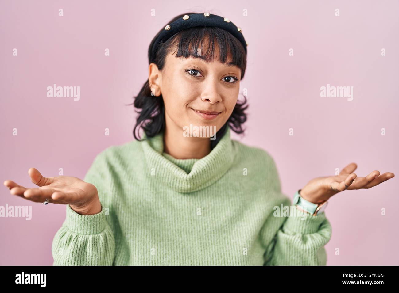 Young beautiful woman standing over pink background clueless and ...