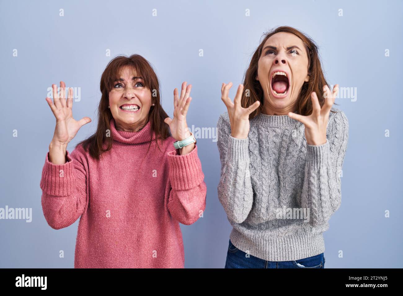 Mother and daughter standing over blue background crazy and mad ...