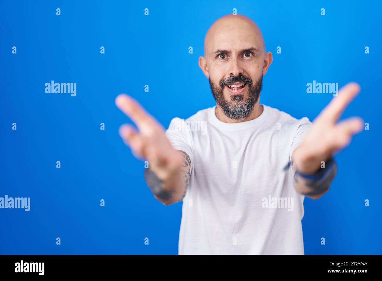 Hispanic man with tattoos standing over blue background smiling ...