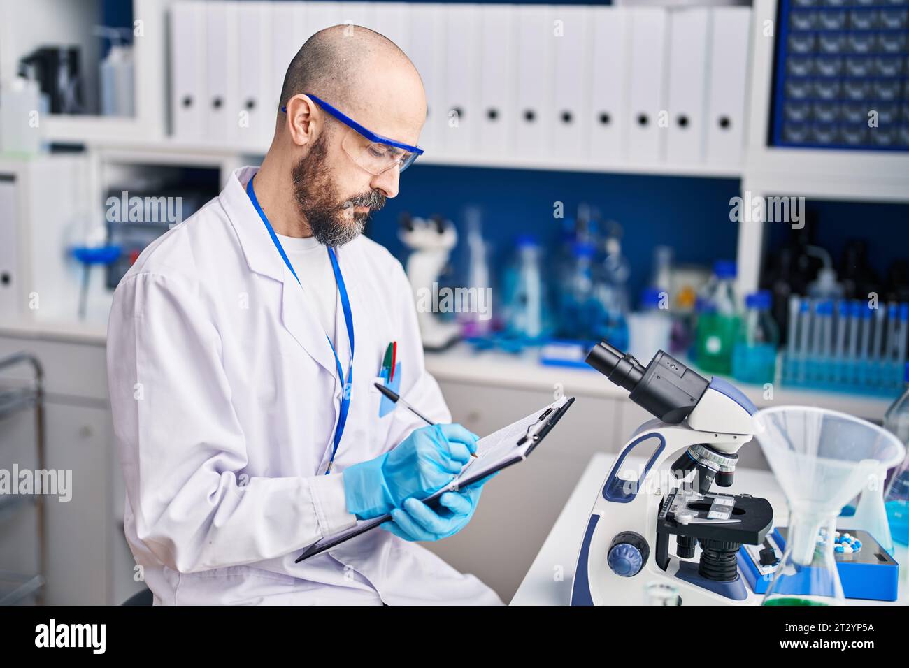 Young bald man scientist writing report working at laboratory Stock ...