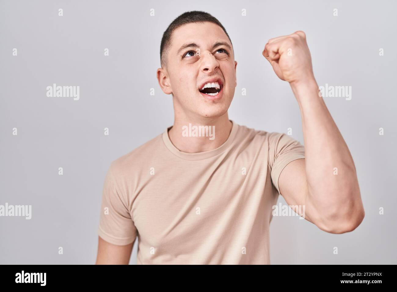 Young man standing over isolated background angry and mad raising fist ...