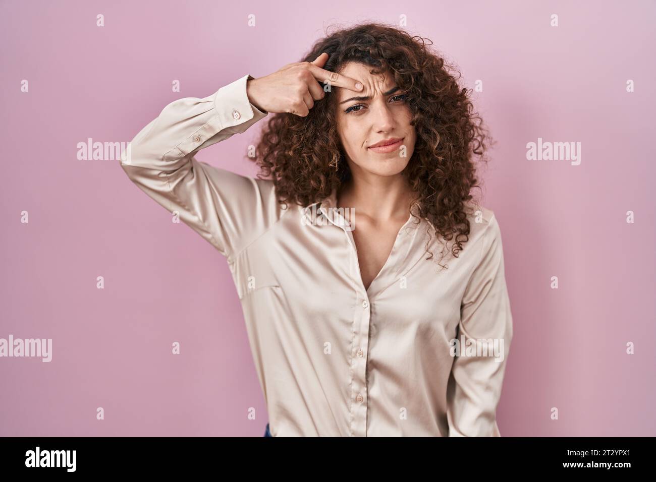 Hispanic woman with curly hair standing over pink background pointing ...