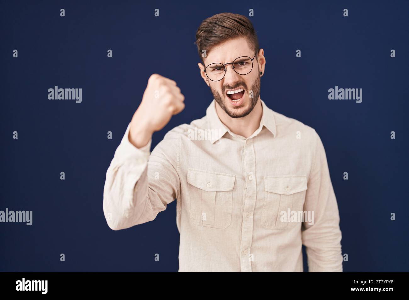 Hispanic man with beard standing over blue background angry and mad ...