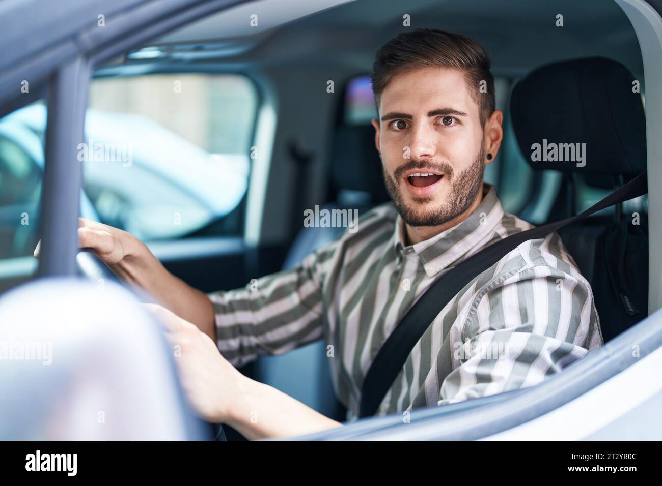 Hispanic man with beard driving car scared and amazed with open mouth ...
