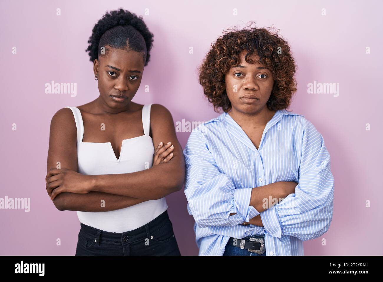Two african women standing over pink background skeptic and nervous ...