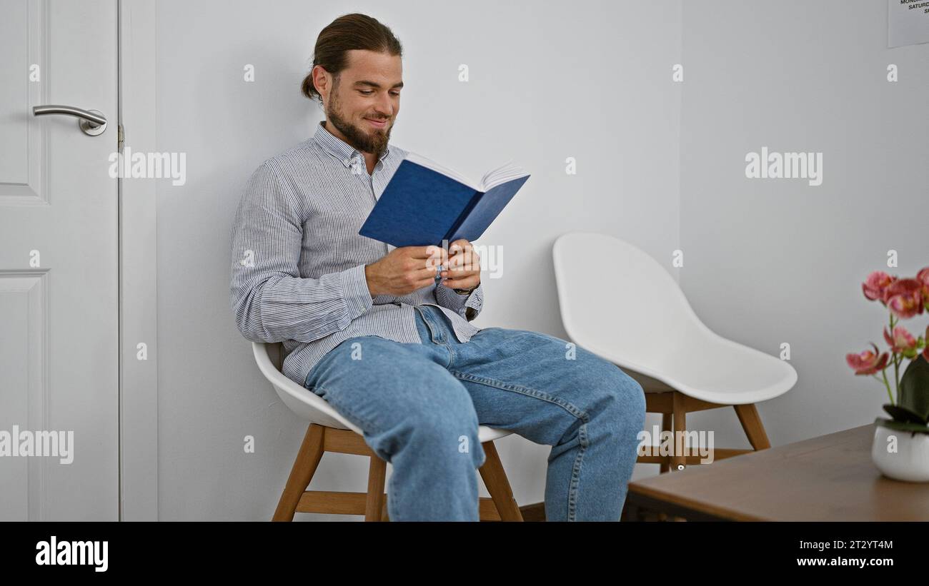 Young hispanic man reading book sitting on chair smiling at waiting ...