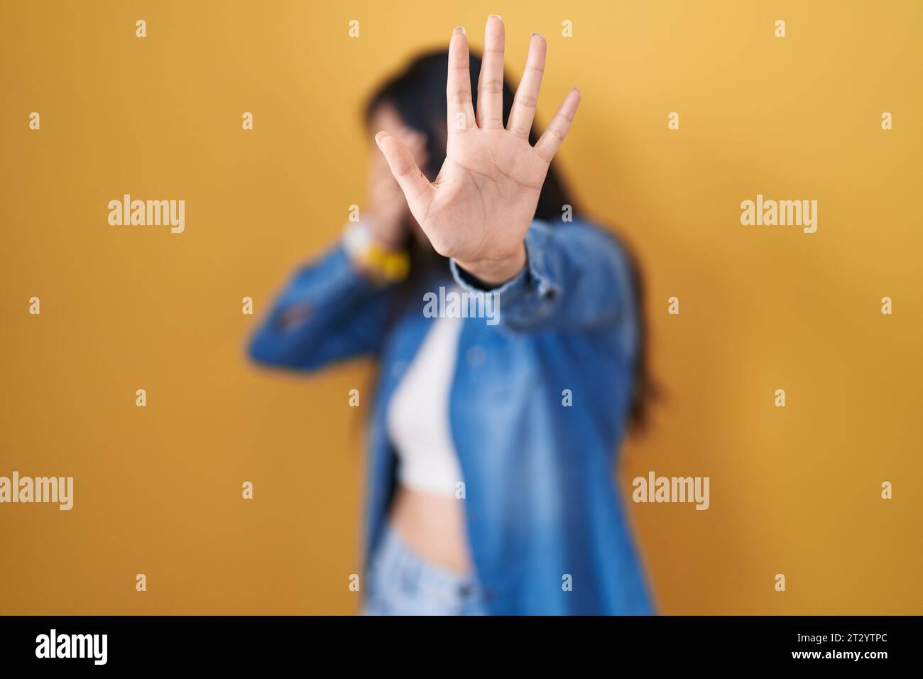 Young asian woman standing over yellow background covering eyes with ...