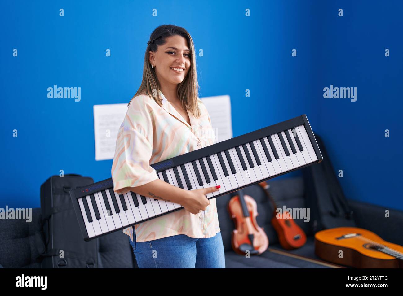 Blonde woman holding piano keyboard looking positive and happy standing ...