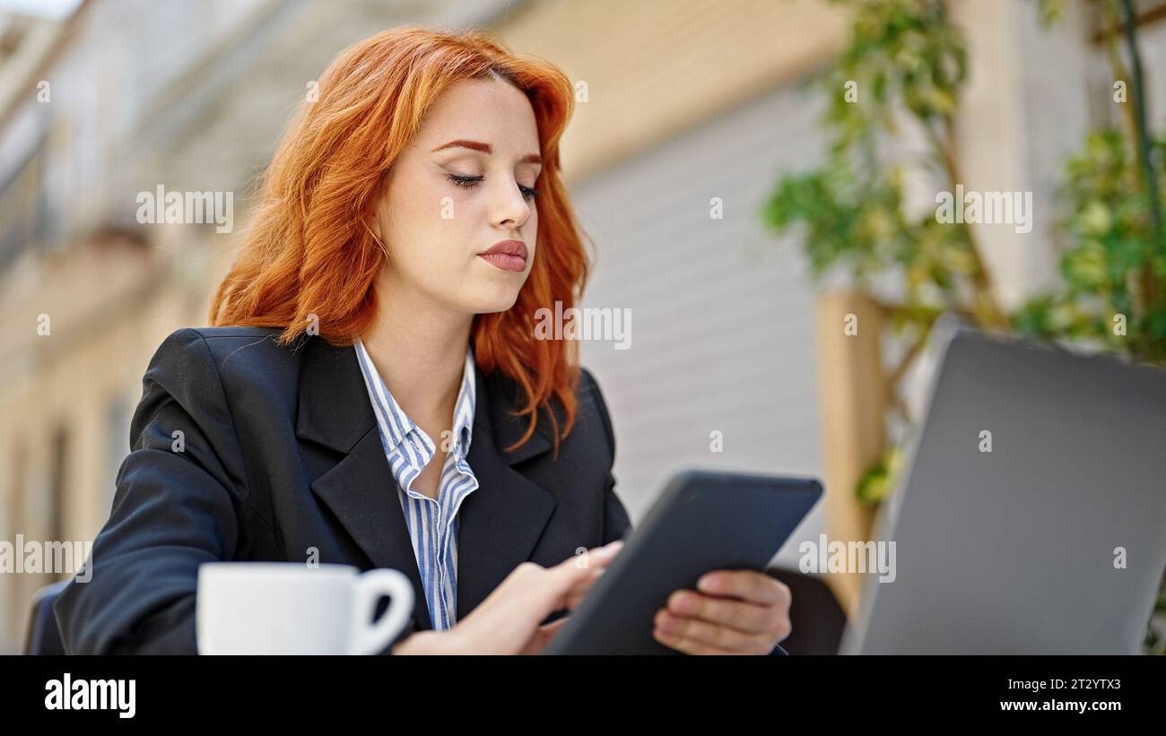 Young redhead woman business worker using laptop and touchpad at coffee ...